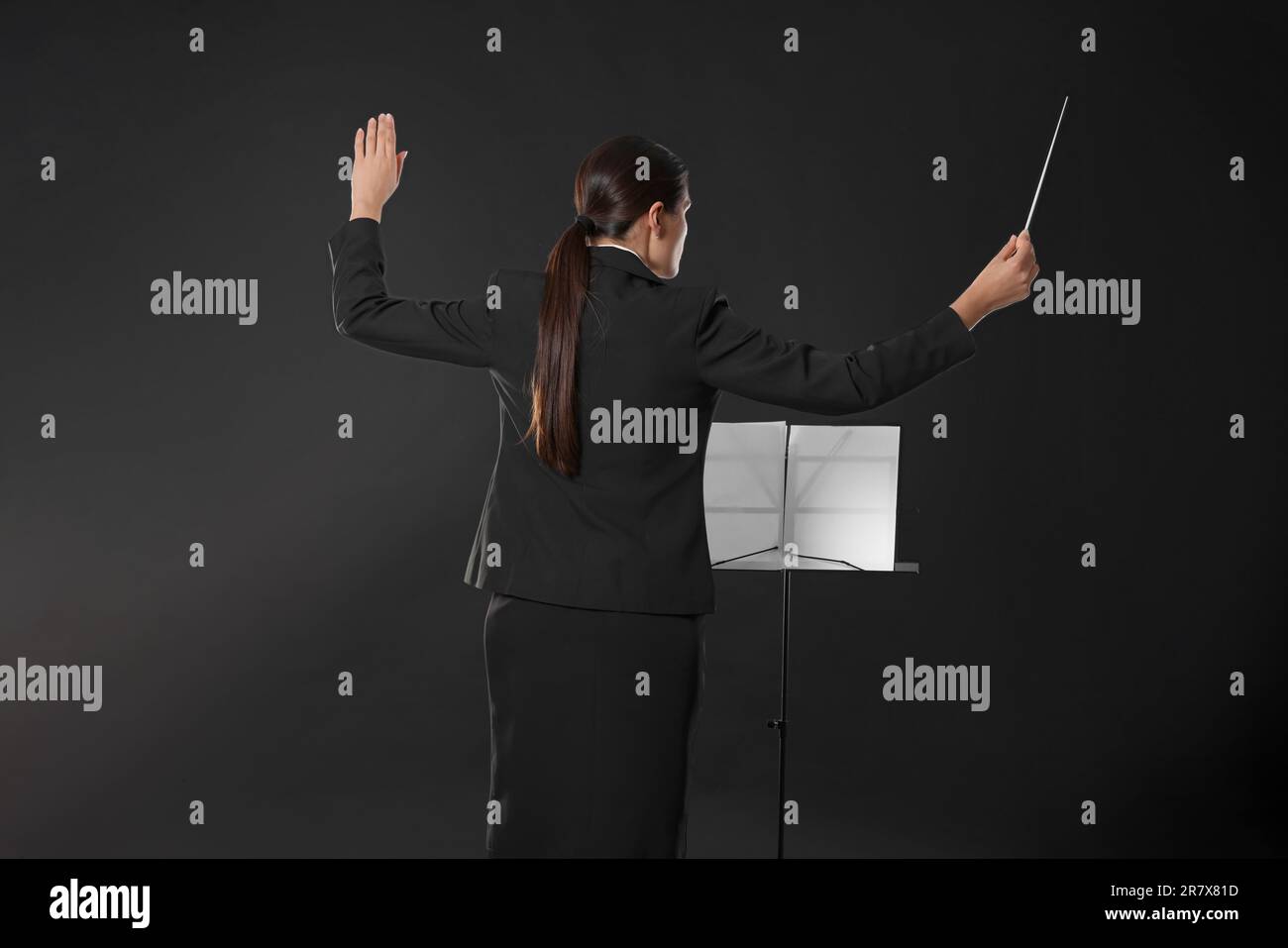 Professional conductor with baton and note stand on dark background ...