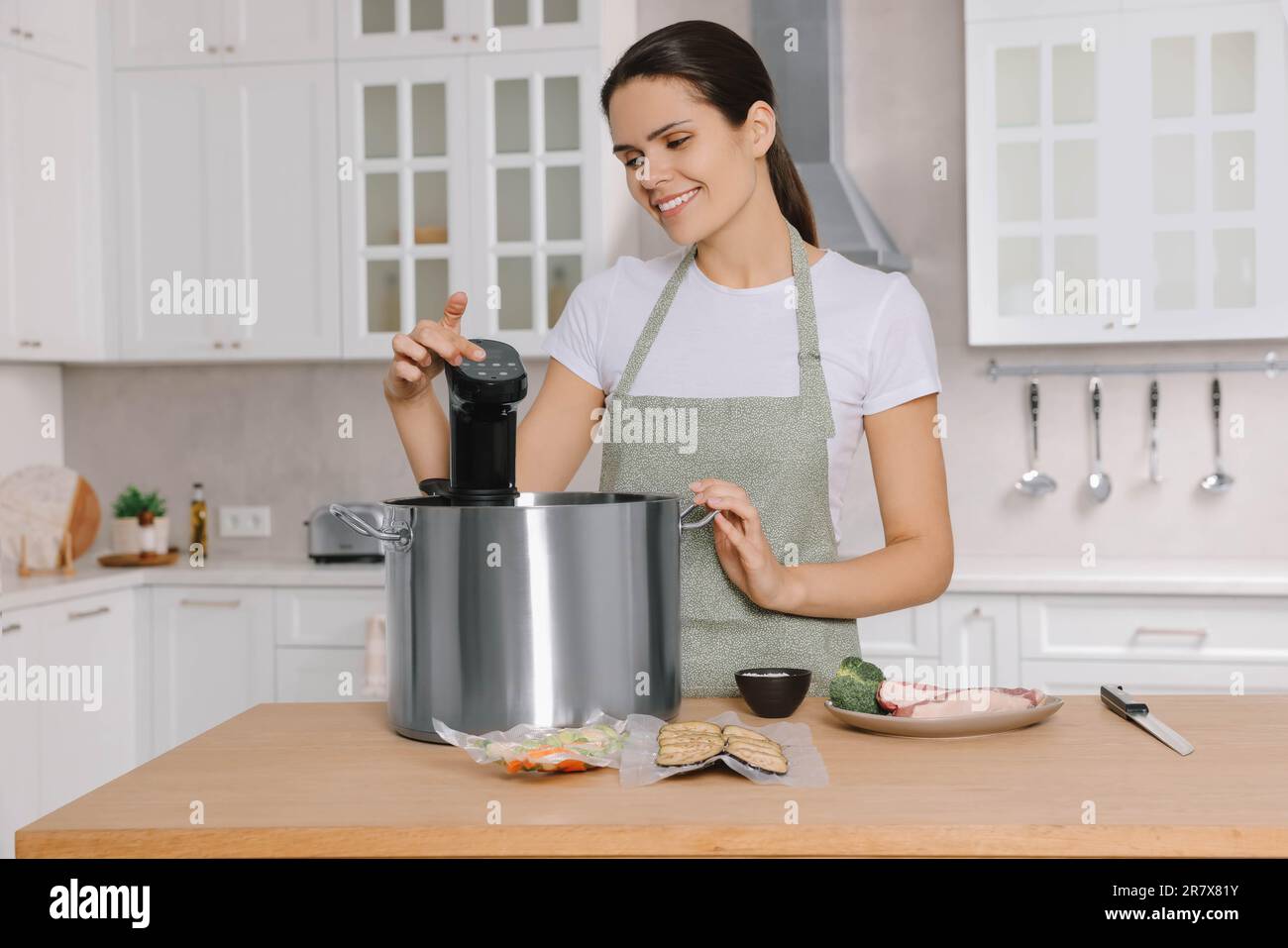Woman using thermal immersion circulator at table in kitchen. Sous vide ...