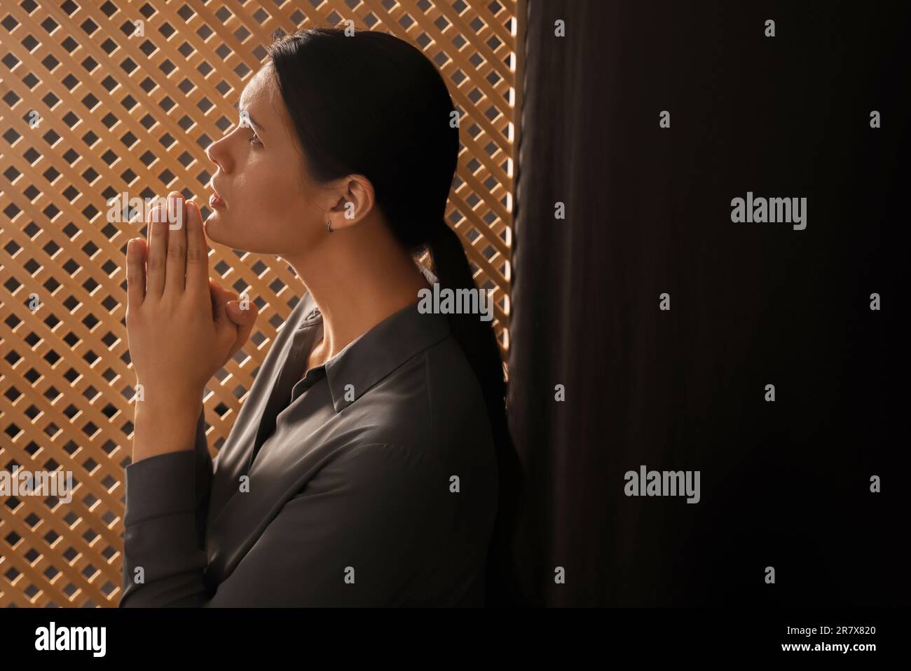 Woman praying to God during confession in booth, space for text Stock ...