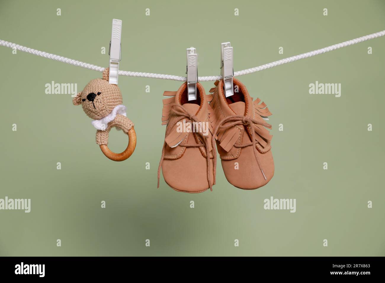 Cute small baby shoes and toy hanging on washing line against green ...