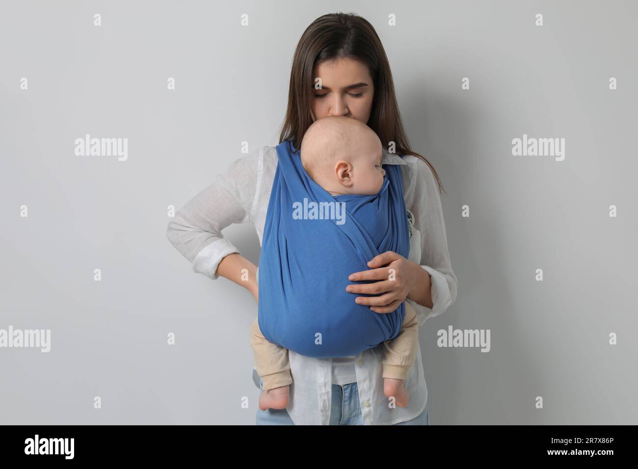 Mother holding her child in sling (baby carrier) on light grey ...