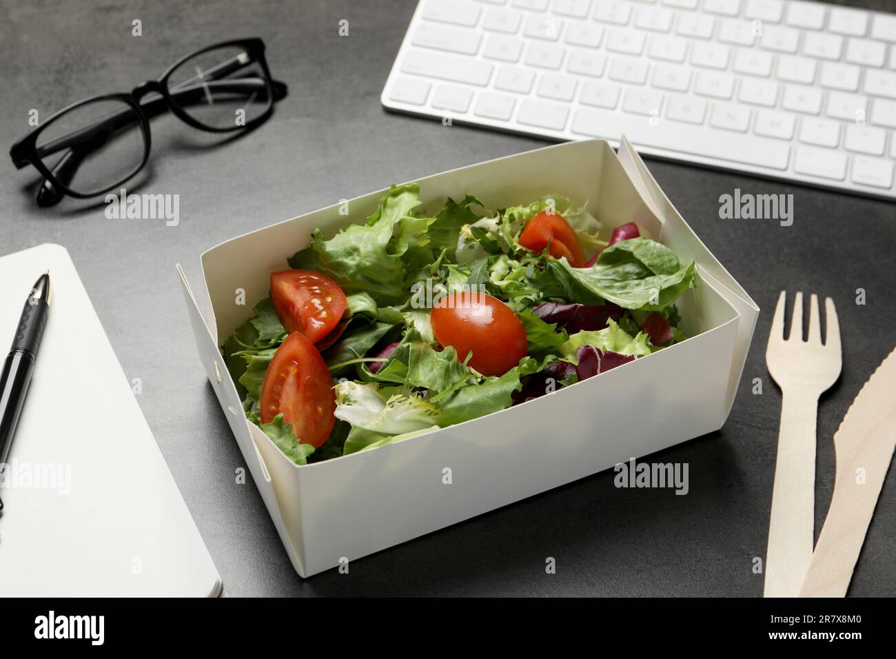 Container of tasty food, keyboard, glasses, cutlery and notebook on ...