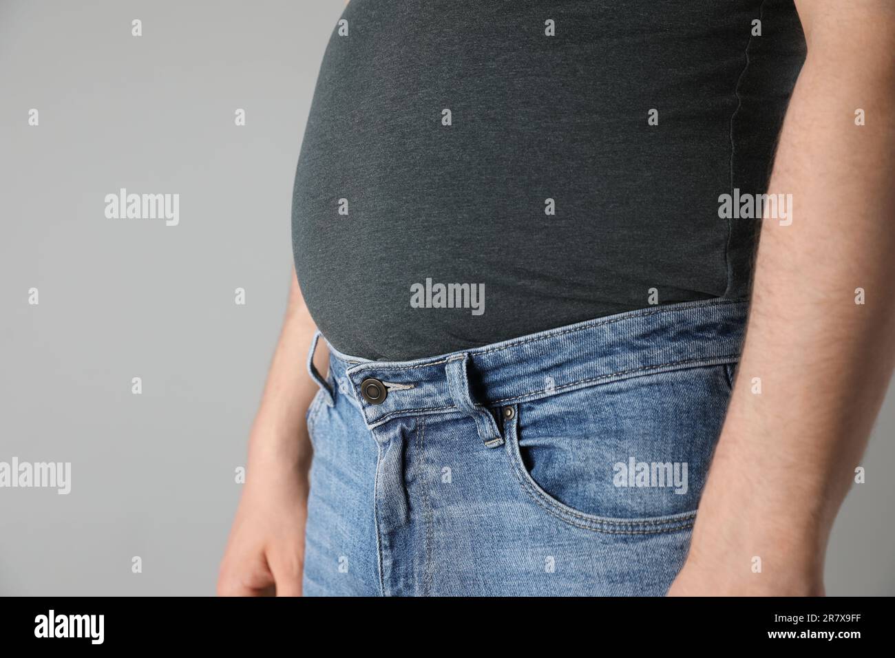 Overweight man in tight tshirt and jeans on light grey background ...
