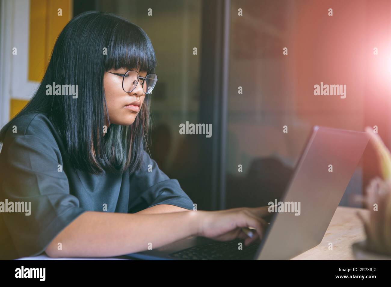 asian teenager sitting in working room and reading message on computer ...