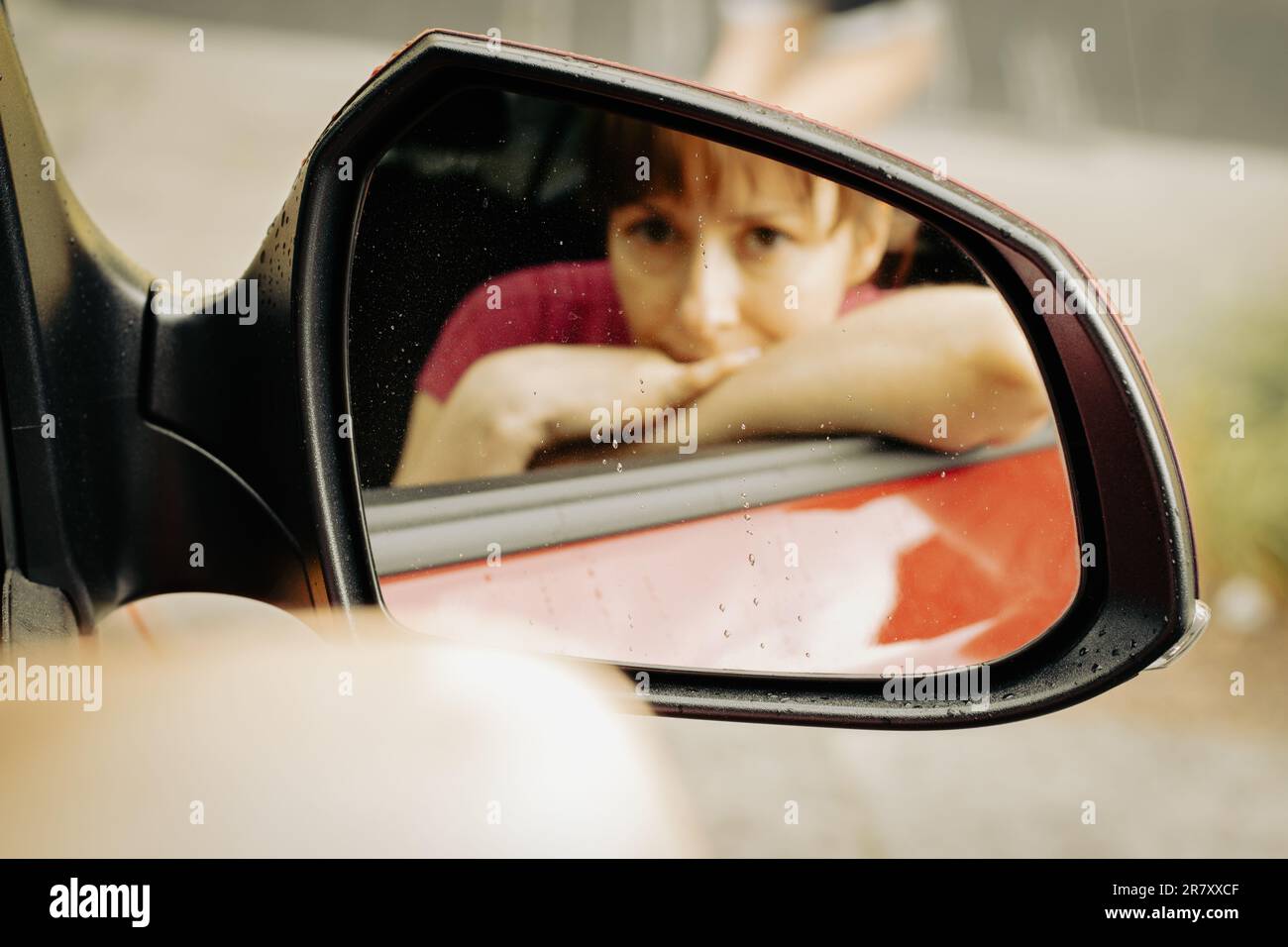 Pretty woman in car window, focus on foreground. Sad girl in car mirror ...