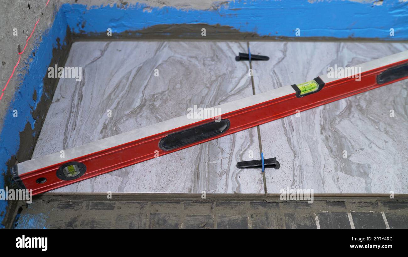A construction technician is working, leveling the tiles on the floor ...