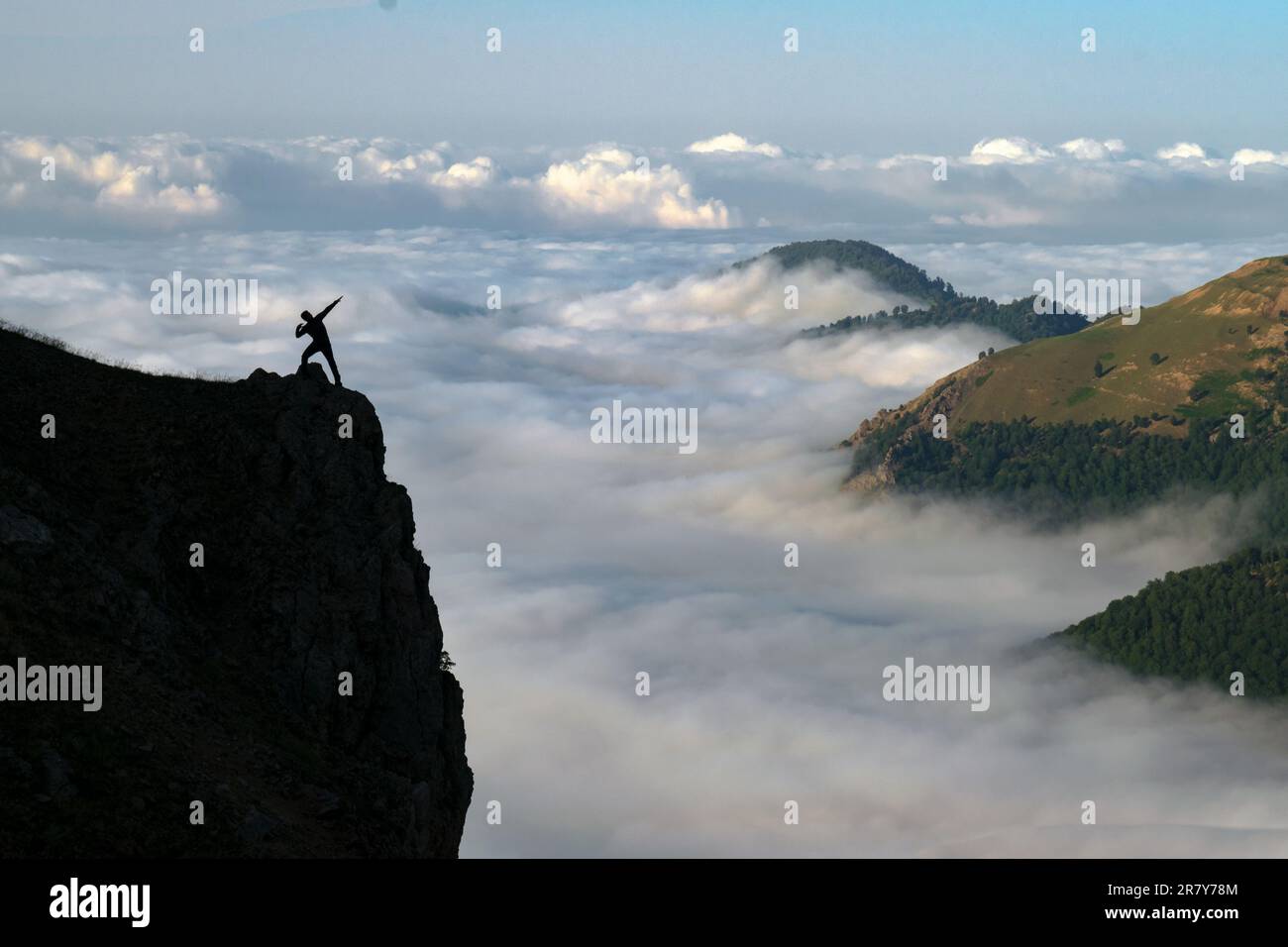 A man stands atop a mountain, his arms raised in a triumphant gesture ...