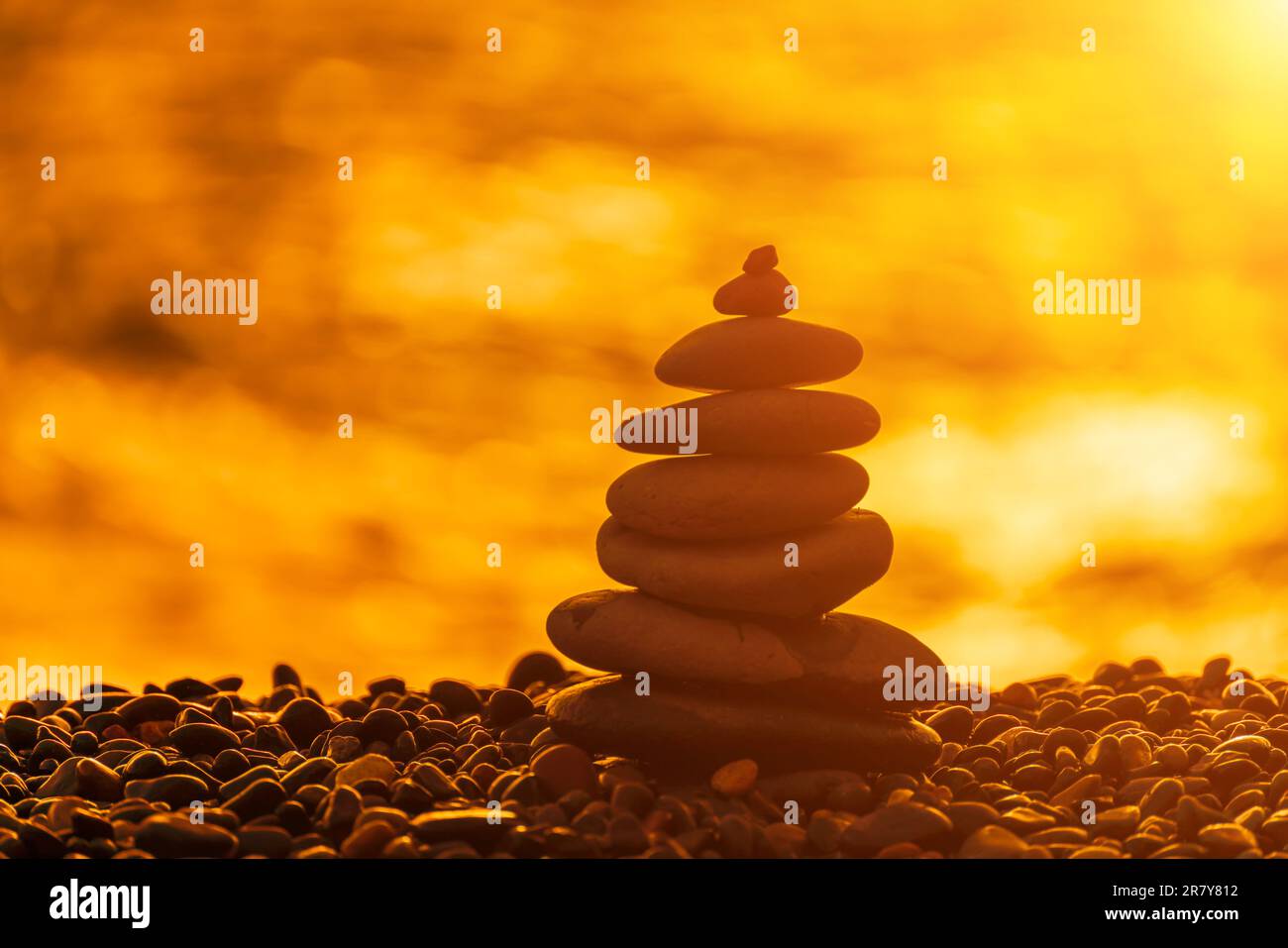Balanced rock pyramid on pebbles beach. Golden sea bokeh on background ...