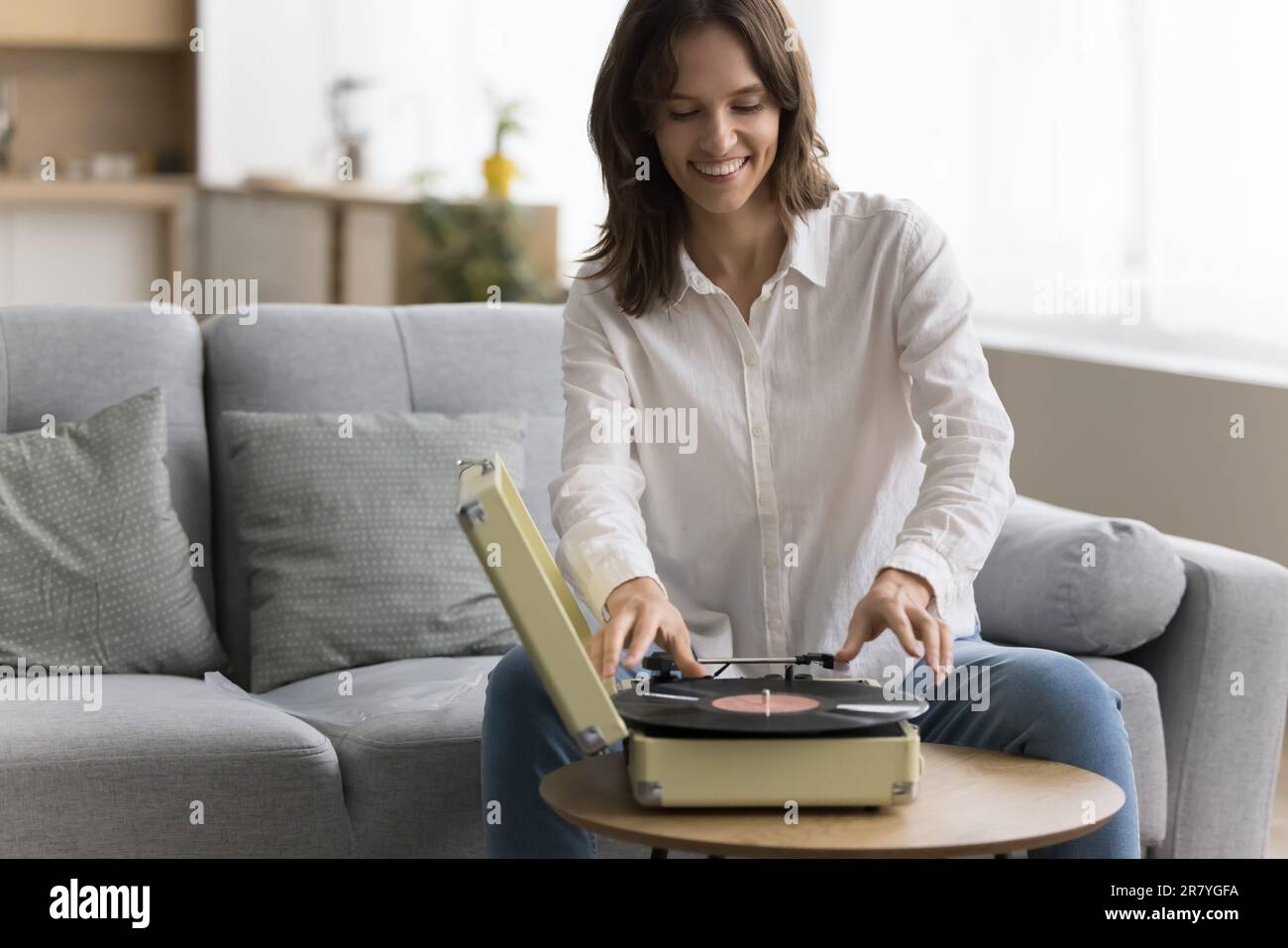 Happy woman placing vinyl record on turntable seated on couch Stock ...