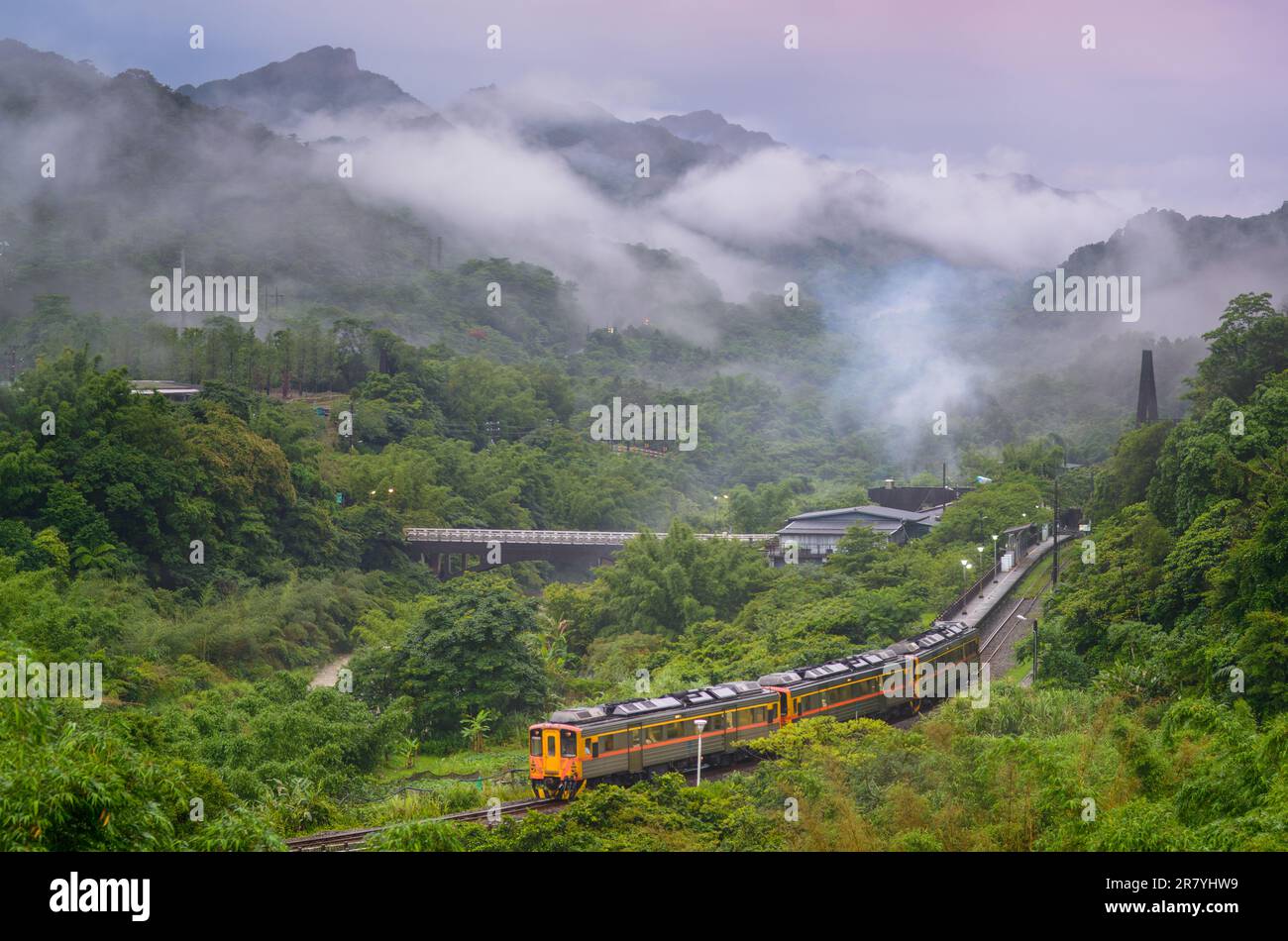 A yellow diesel train is driving in the mountains and forests. Along ...