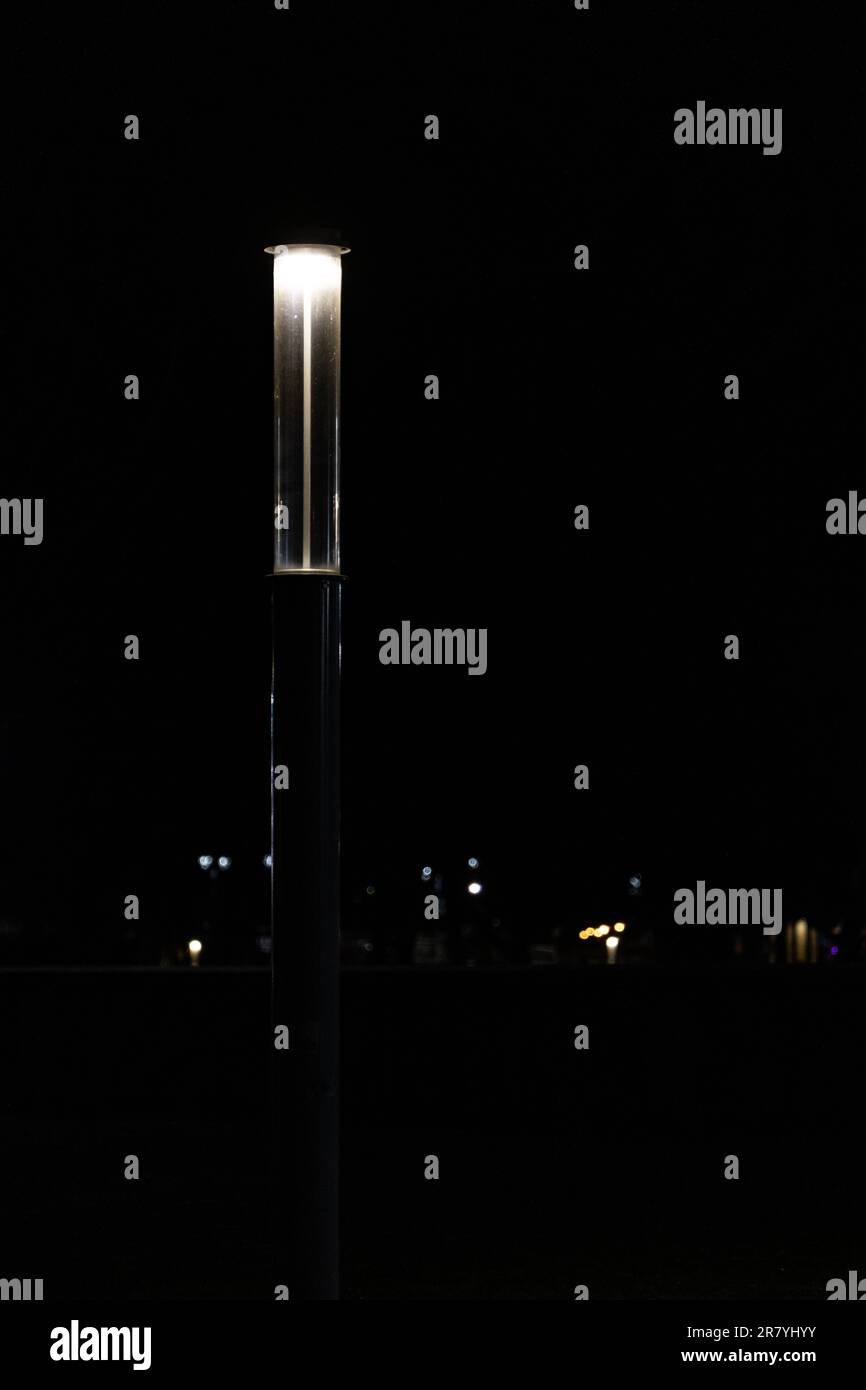 A vertical shot of a street light at night with the city lights on ...