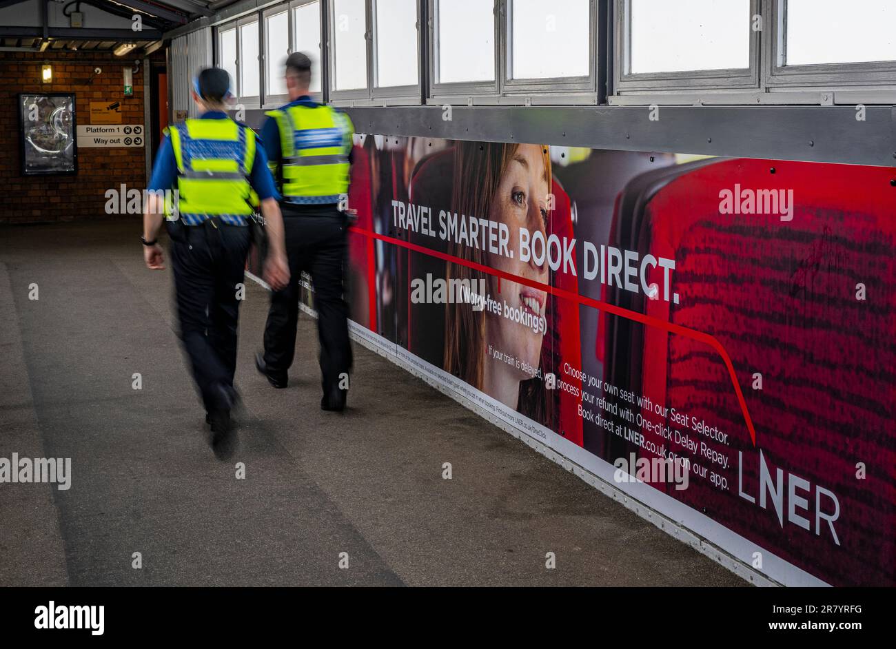 British Transport Police policemen walking past an advertising hoarding ...