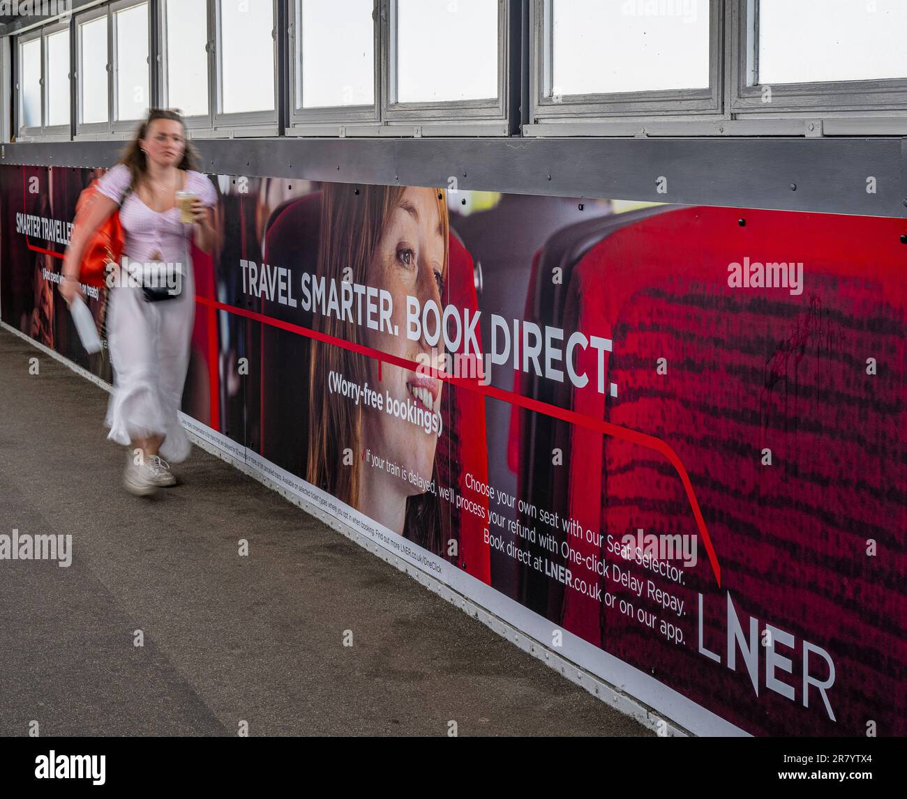 A young woman walking past an advertising hoarding for London North Eastern Railway (LNER) for ...