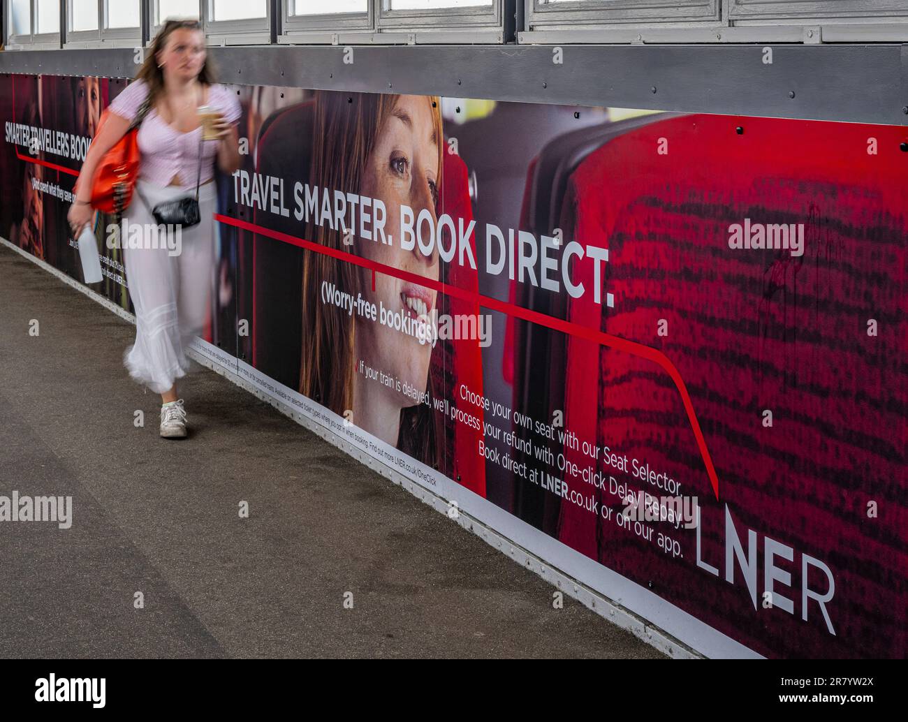 A young woman walking past an advertising hoarding for London North ...