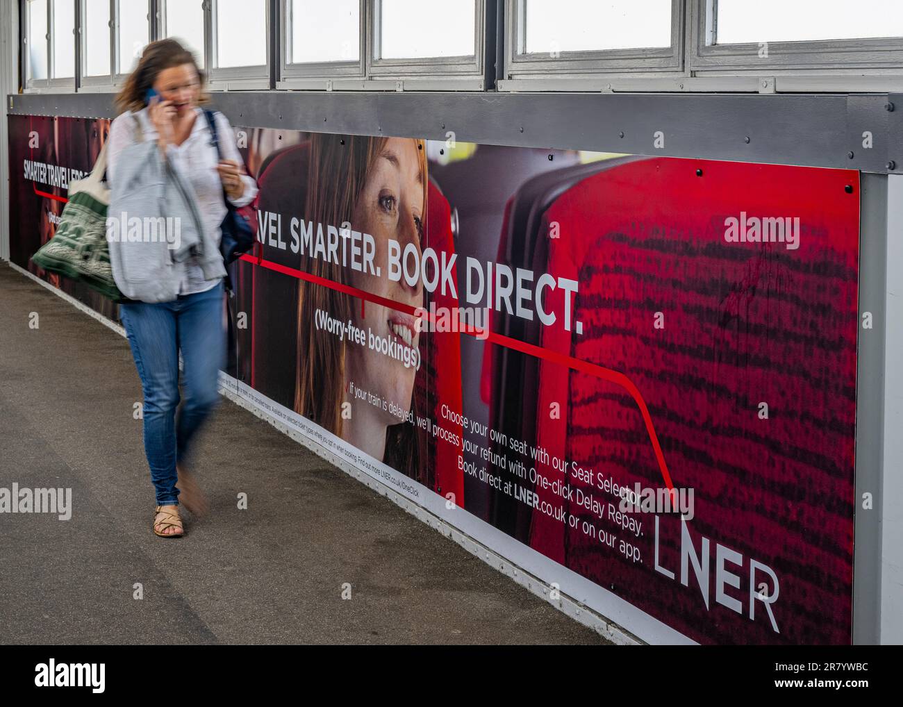 Woman on mobile phone walking past an advertising hoarding for London North Eastern Railway ...