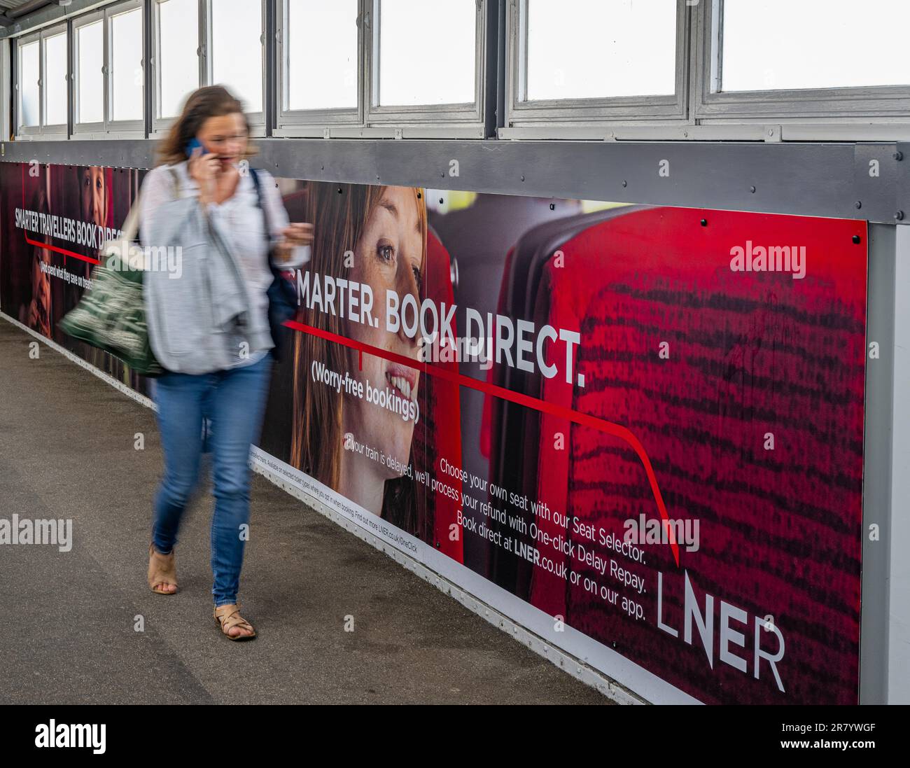 Woman on mobile phone walking past an advertising hoarding for London North Eastern Railway ...