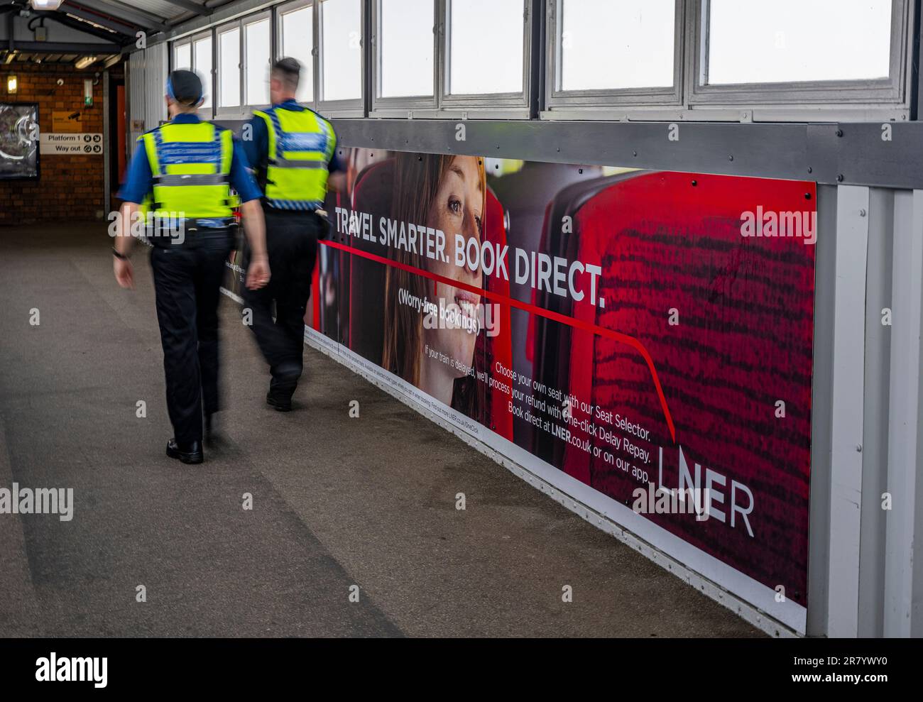 British Transport Police policemen walking past an advertising hoarding ...