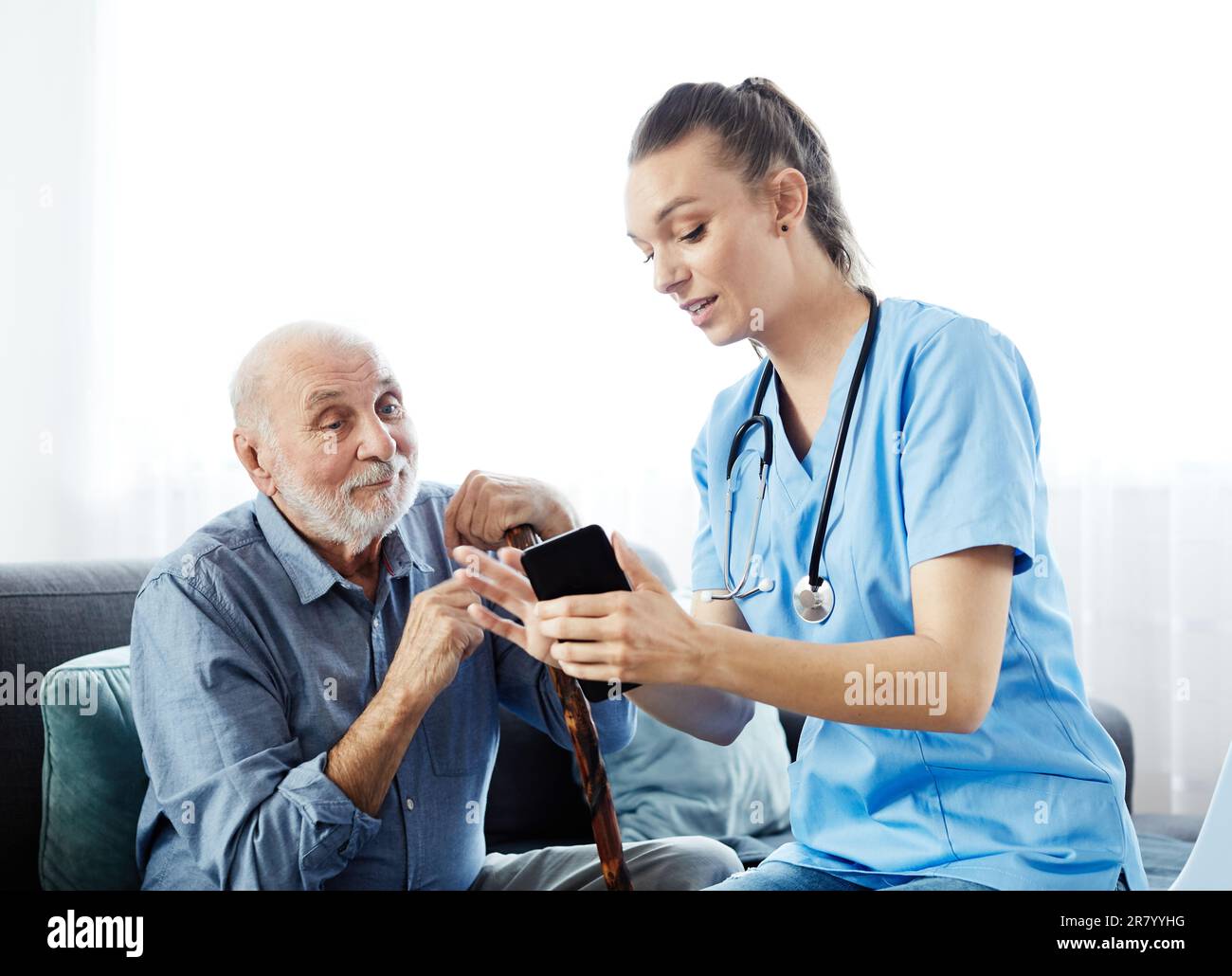 Doctor or nurse caregiver helping senior man with a mobile phone at ...
