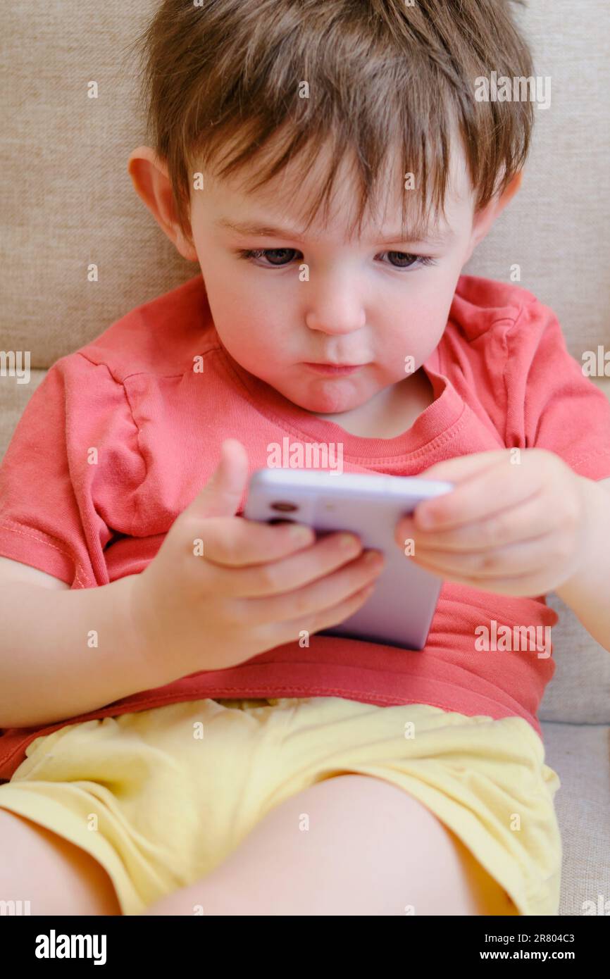 Toddler is busy tapping the phone screen. The phone-holding child looks ...