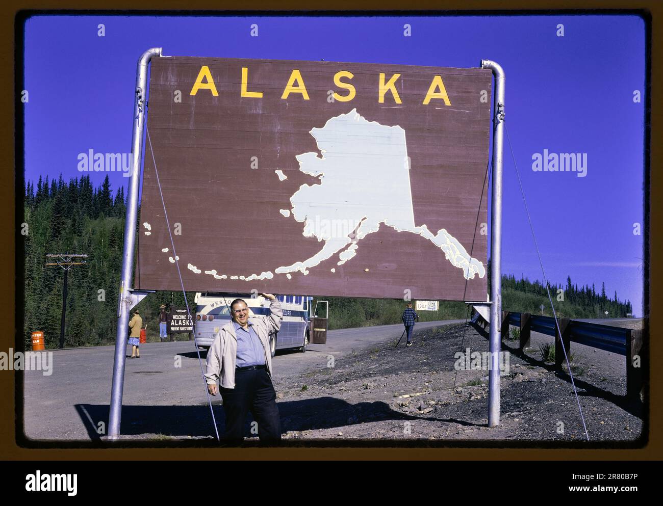 Alaska State Sign 1967. Man pretending to hold up sign with tourist bus ...