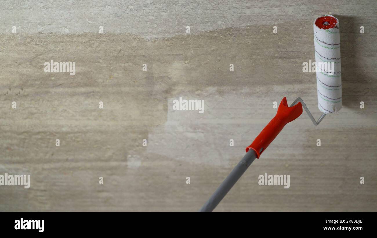 A worker applies paint to the ceiling with a hand roller at home ...