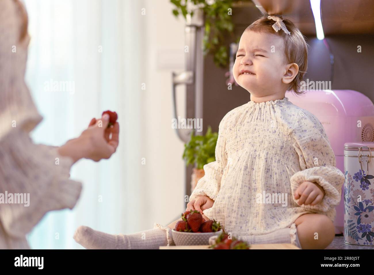 Mom feeding her baby girl with sour strawberries in the kitchen ...