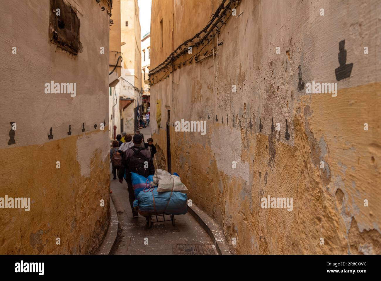 A person pulling a cart through a narrow typical alley of the medina of ...
