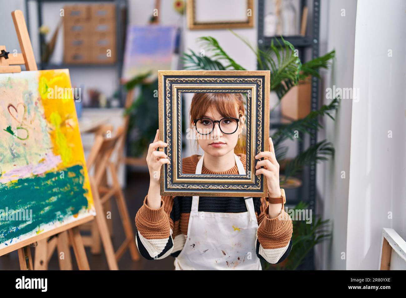 Young beautiful artist woman with face inside empty vintage frame ...