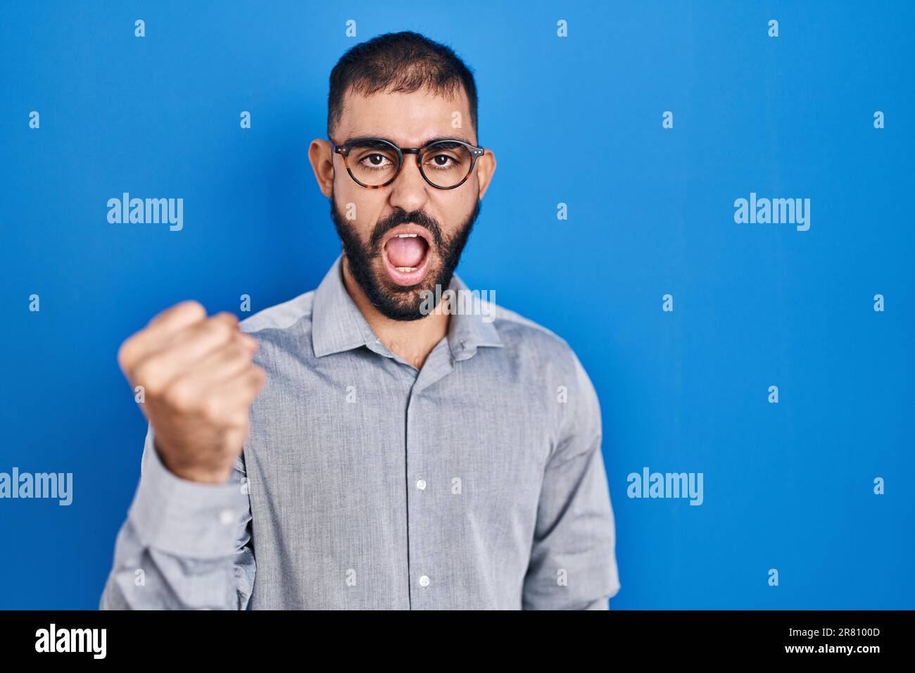 Middle east man with beard standing over blue background angry and mad ...