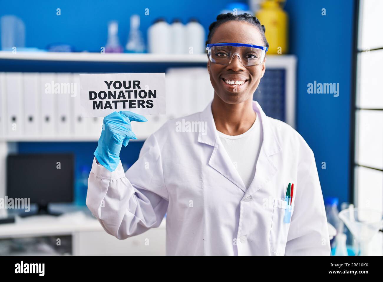 Beautiful black woman working at scientist laboratory holding your donation matters banner ...