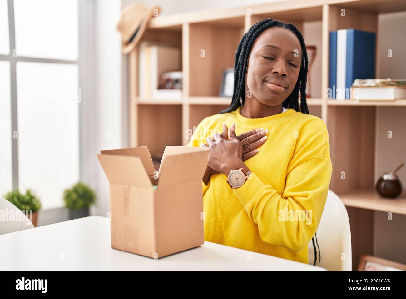 Beautiful black woman opening cardboard box smiling with hands on chest ...