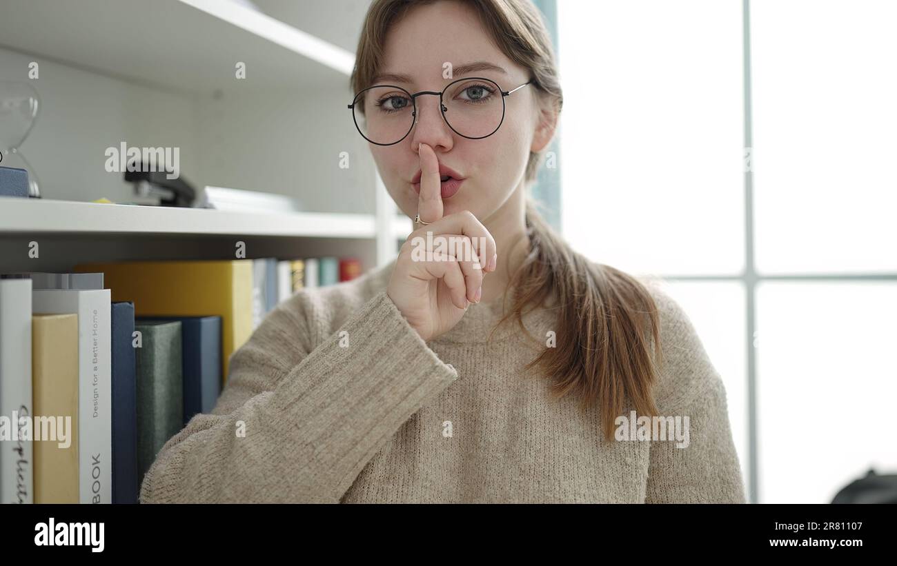Young blonde woman student doing silence gesture at library university ...