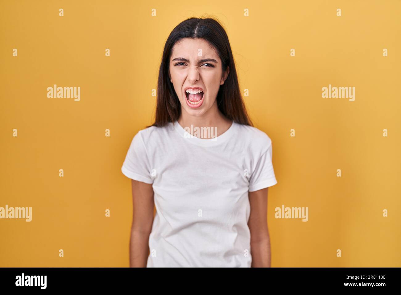 Young beautiful woman standing over yellow background angry and mad ...
