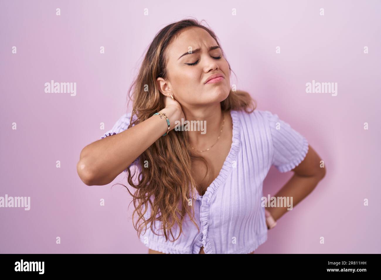 Young hispanic woman standing over pink background suffering of neck ...