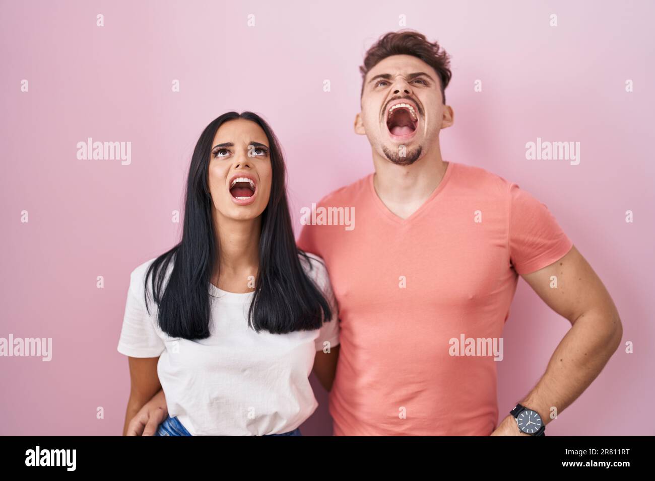 Young hispanic couple standing over pink background angry and mad ...