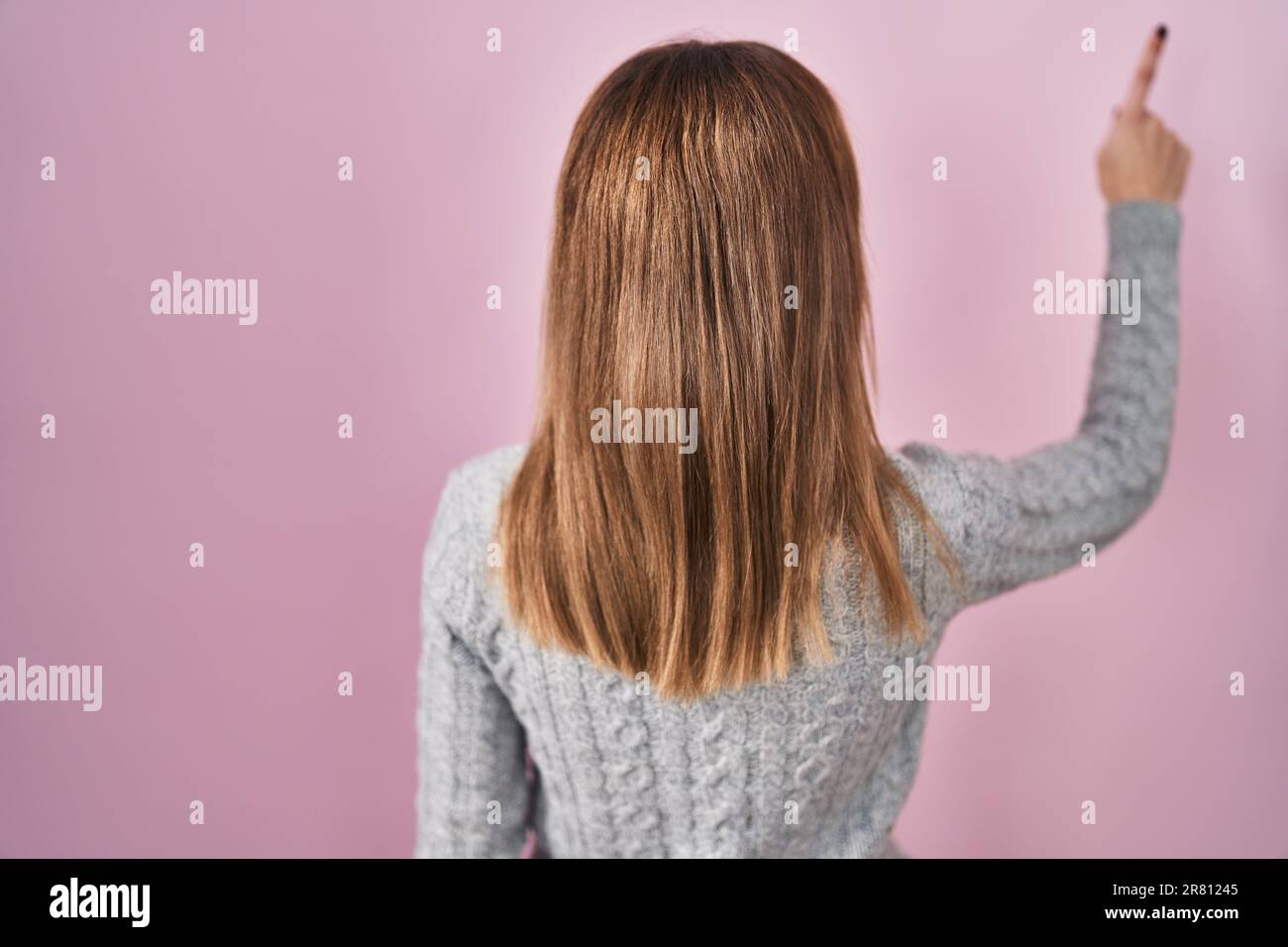 Beautiful woman standing over pink background posing backwards pointing ...