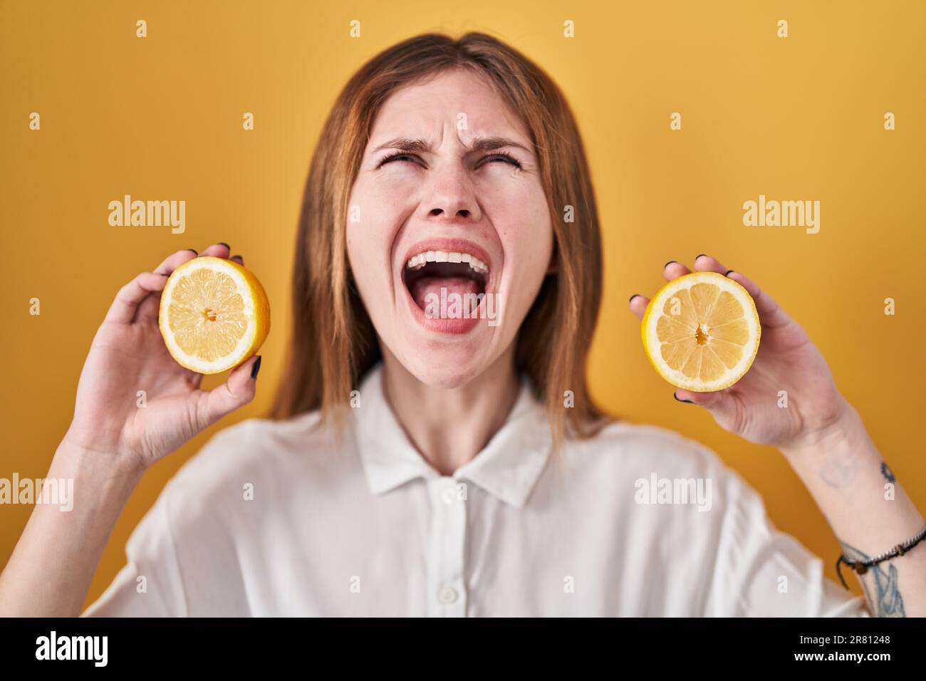 Beautiful woman holding lemons angry and mad screaming frustrated and ...