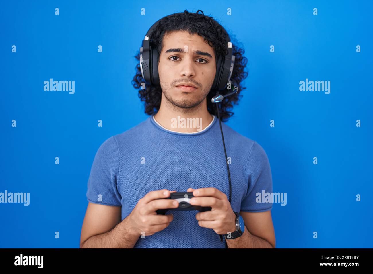 Hispanic man with curly hair playing video game holding controller ...