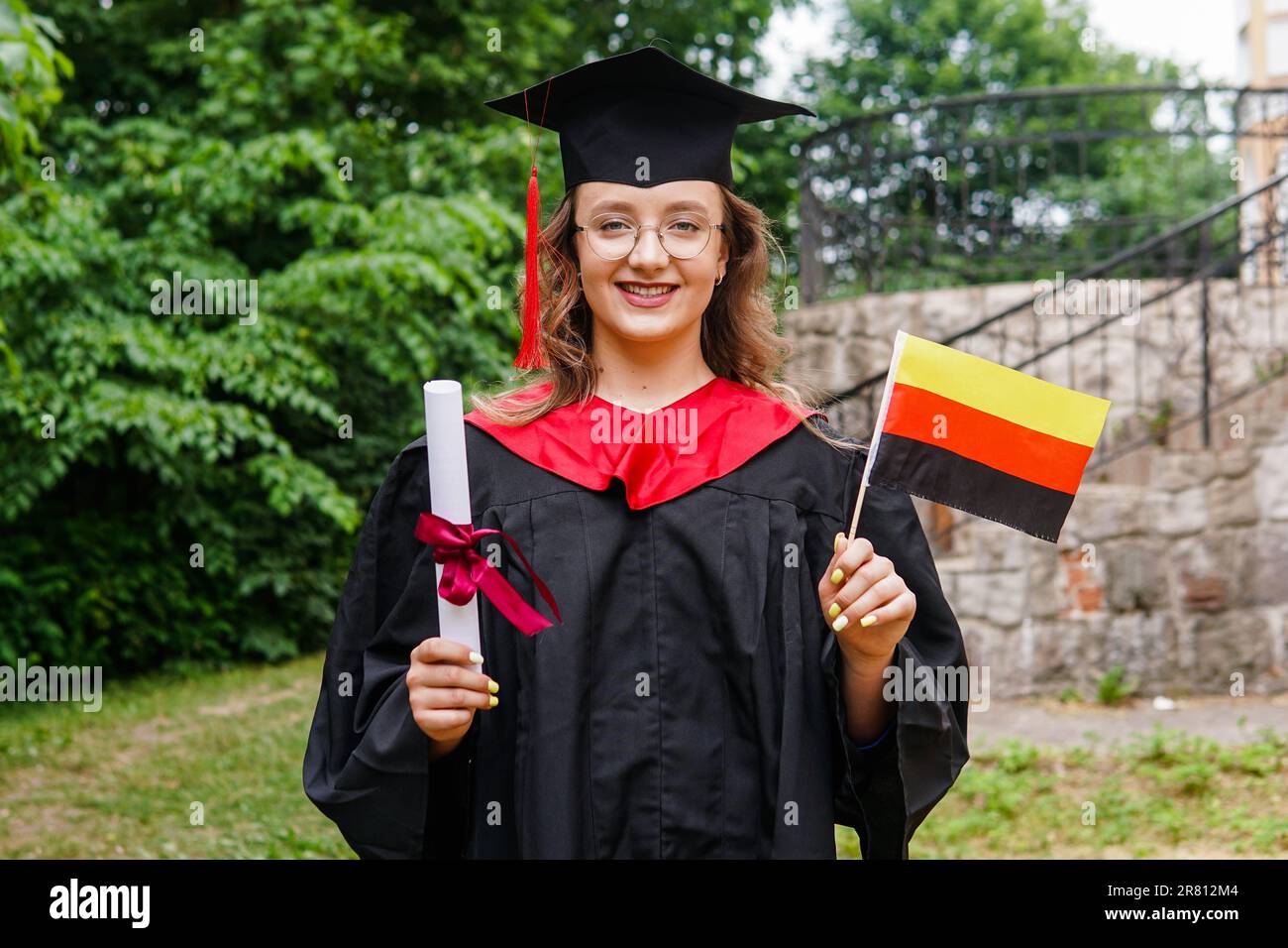 Young german woman wearing graduation gown and hat holding flag of ...