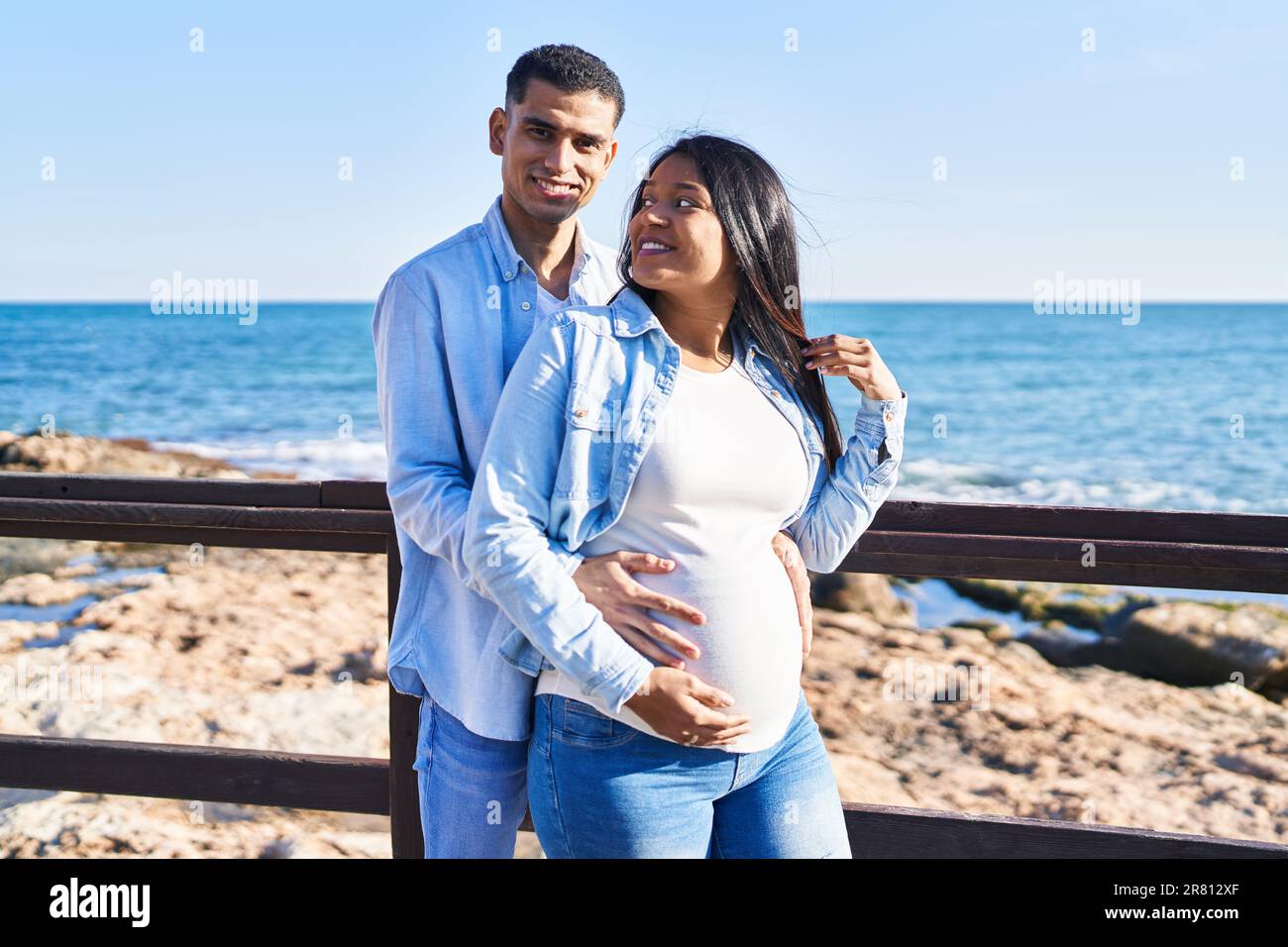 Young latin couple expecting baby hugging each other standing at ...