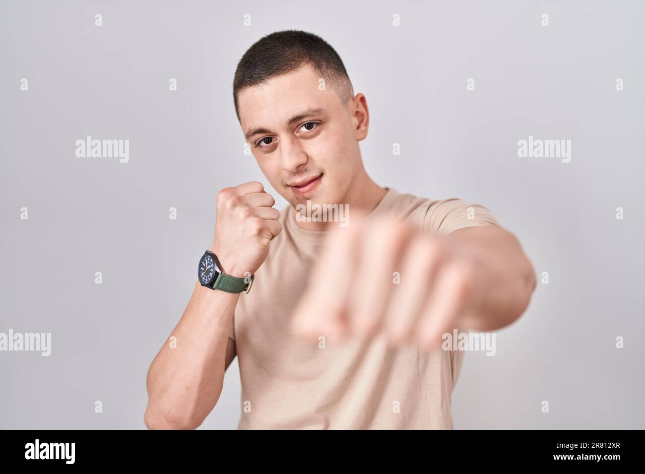 Young man standing over isolated background punching fist to fight ...