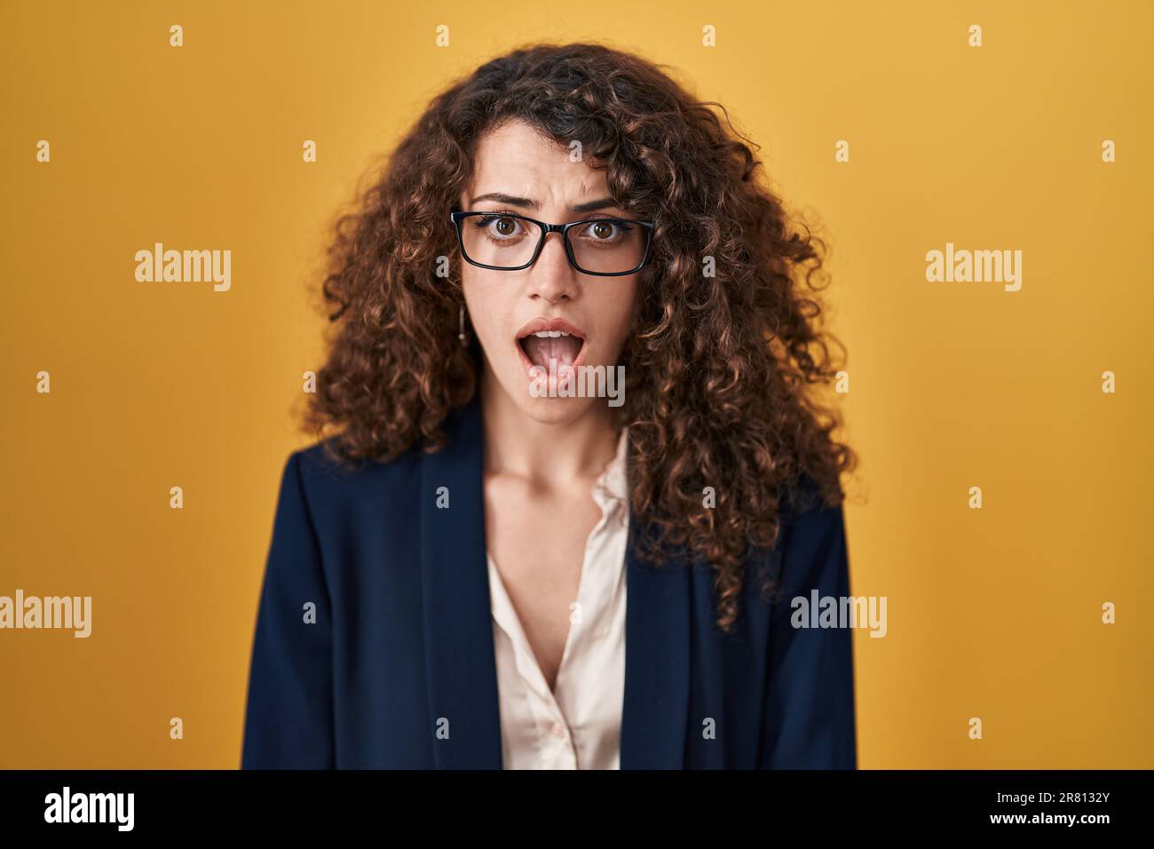 Hispanic woman with curly hair standing over yellow background afraid ...