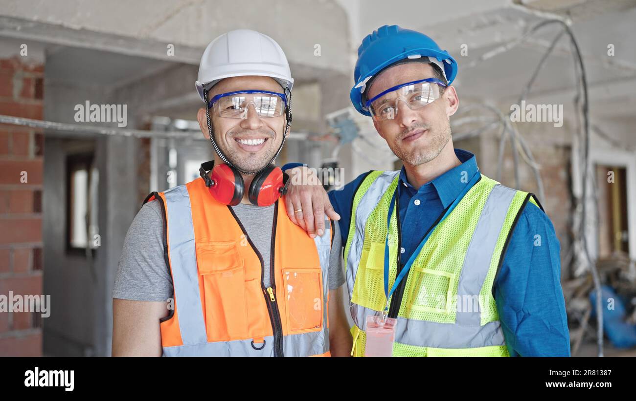 Two men builders smiling confident standing together at construction ...