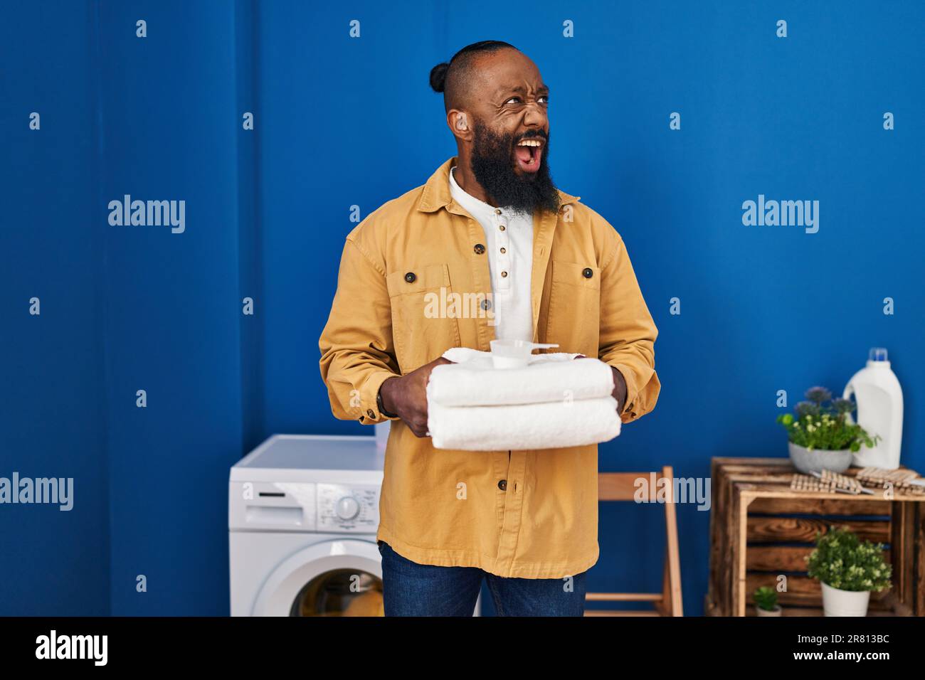 African american man holding clean towels at laundry room angry and mad ...