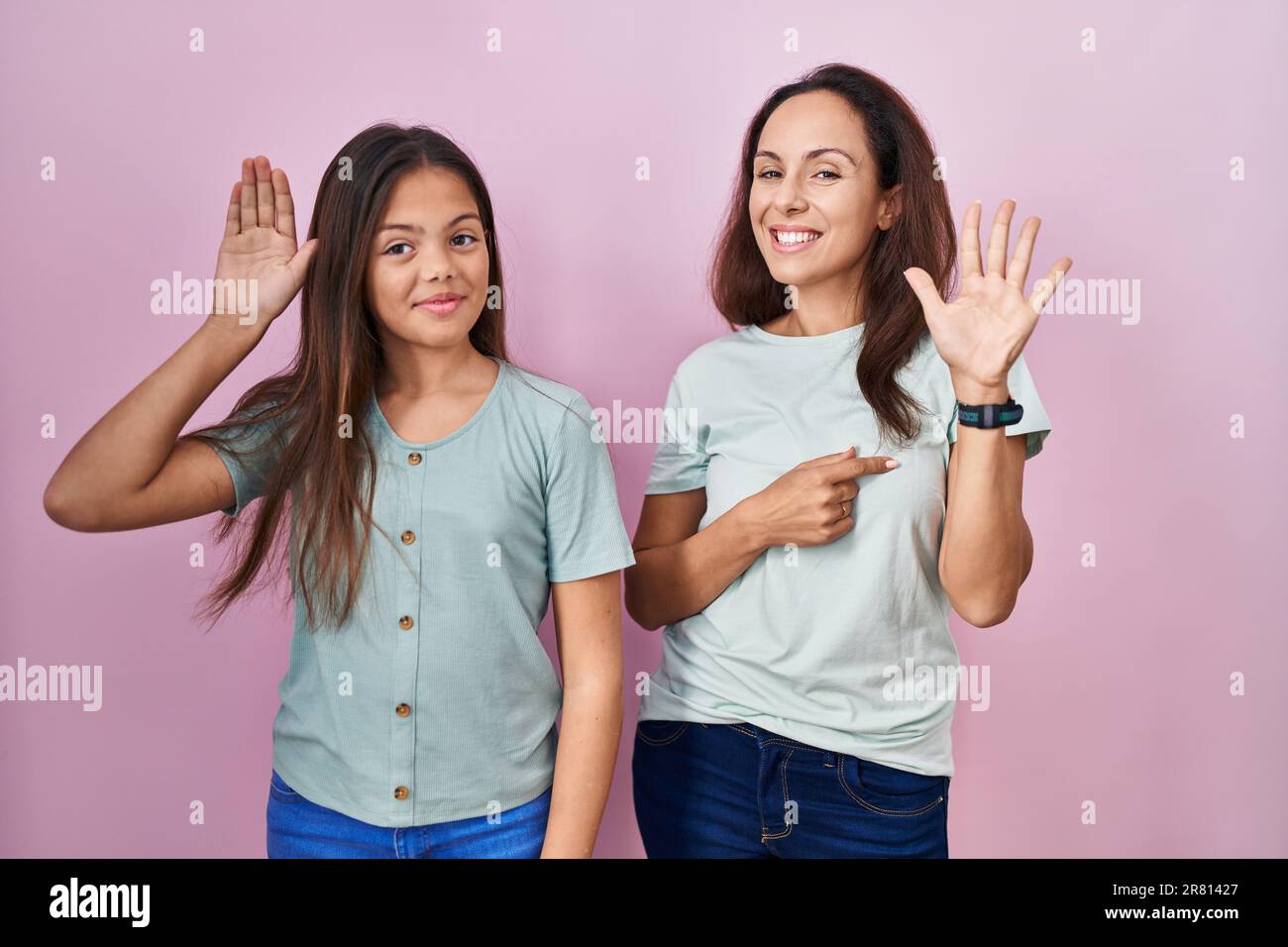 Young Mother And Daughter Standing Over Pink Background Waiving Saying