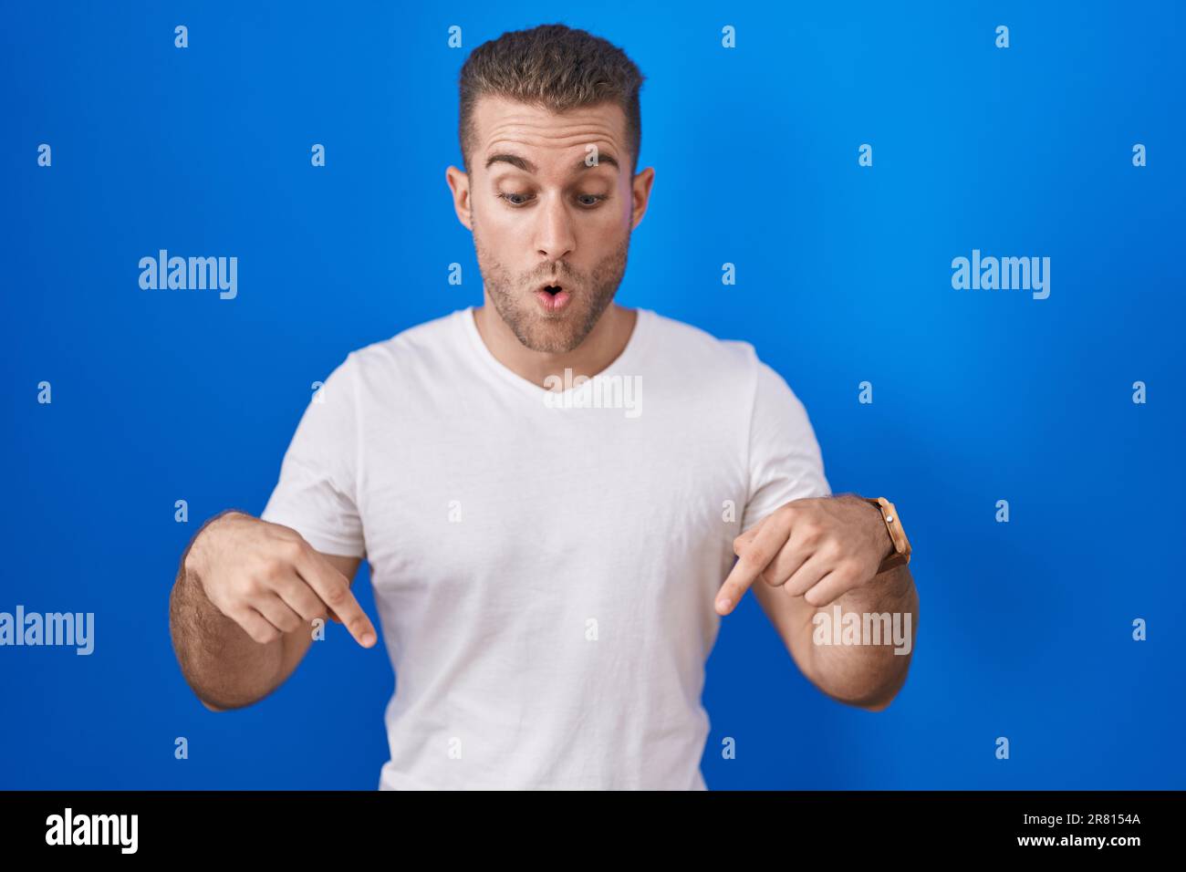 Young caucasian man standing over blue background pointing down with ...
