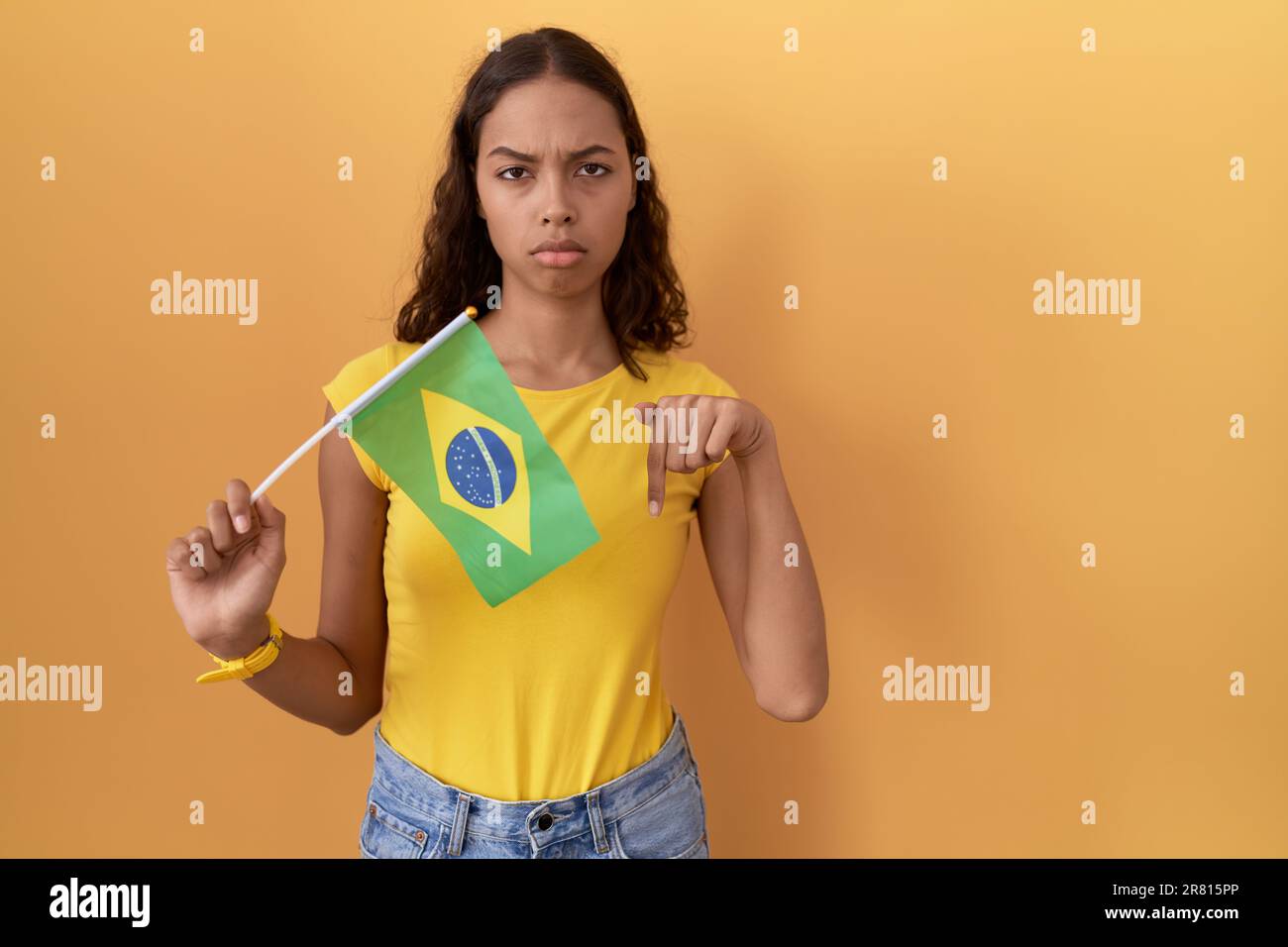 Young hispanic woman holding brazil flag pointing down looking sad and ...