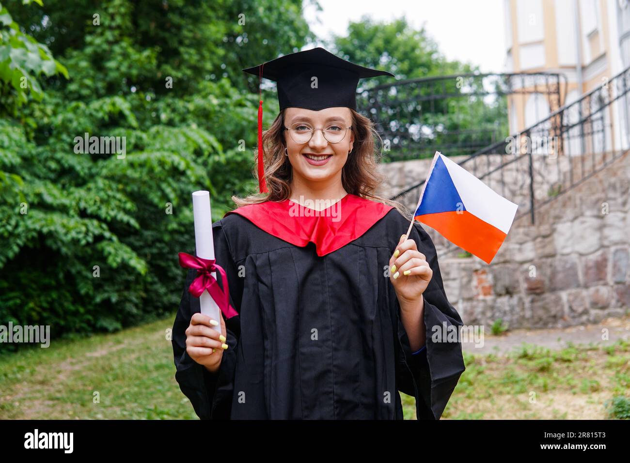 Young czech girl wearing graduation gown and hat holding flag of Czech ...
