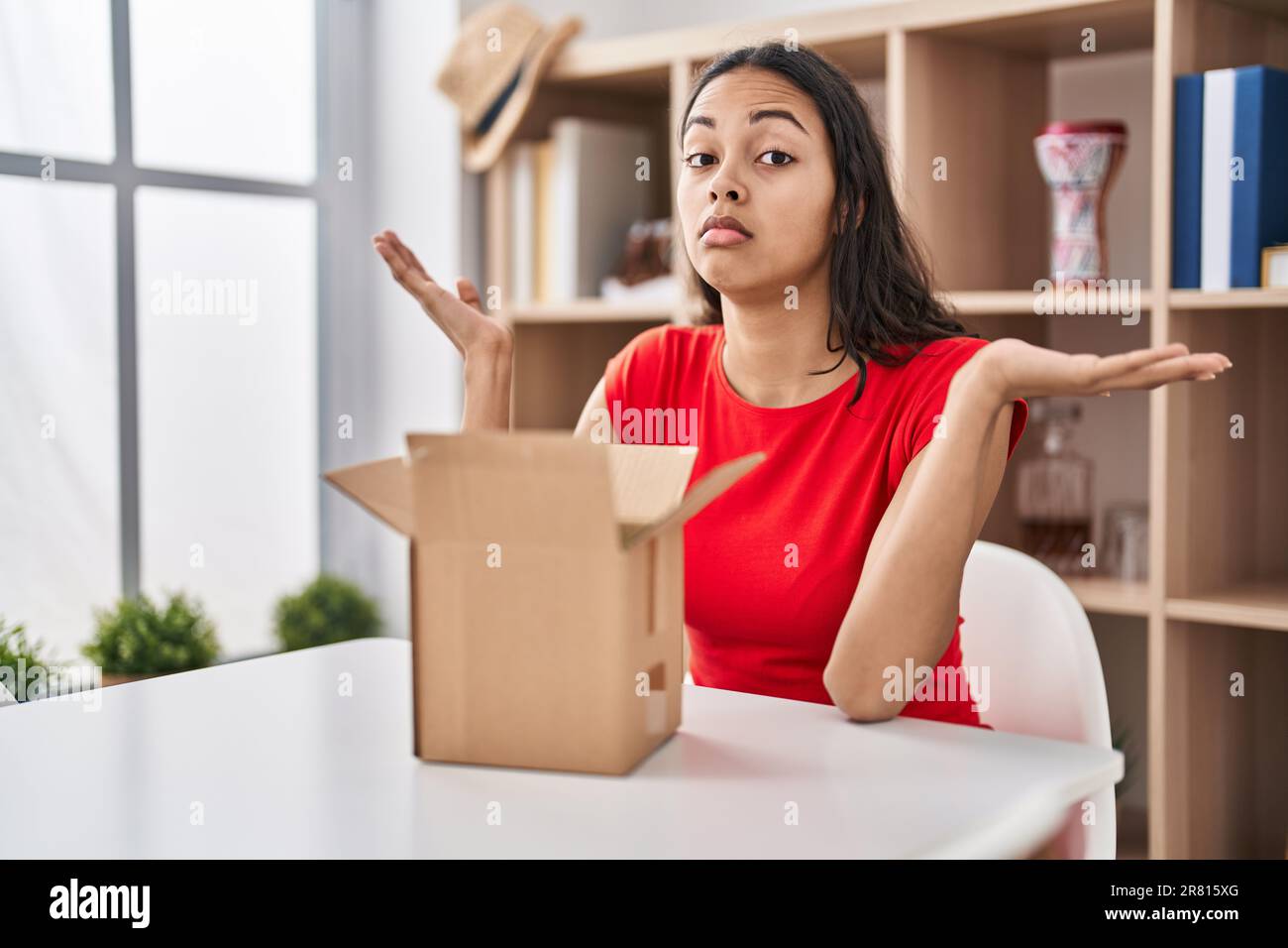 Young brazilian woman looking inside cardboard box shouting and ...