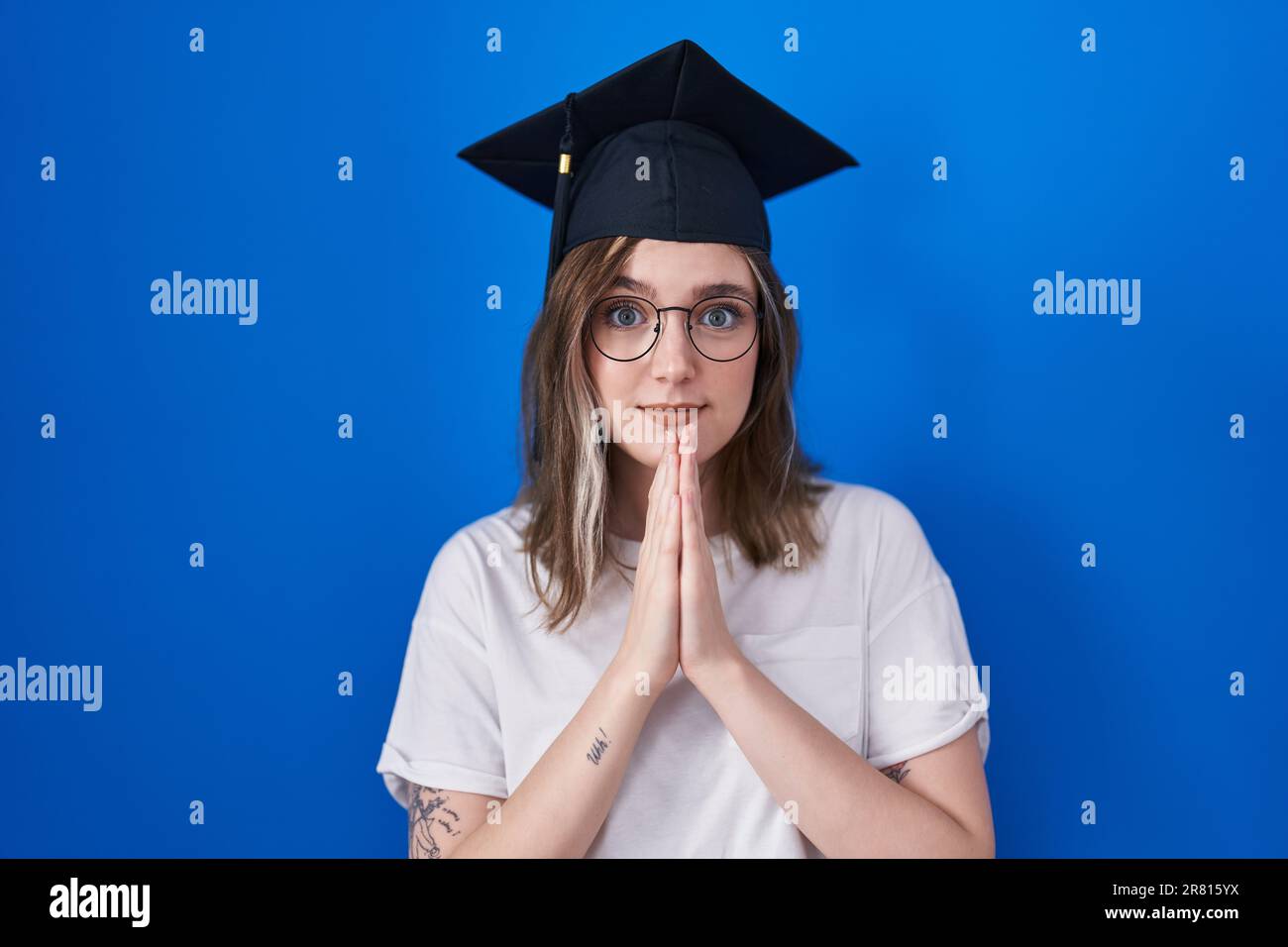 Blonde caucasian woman wearing graduation cap praying with hands ...